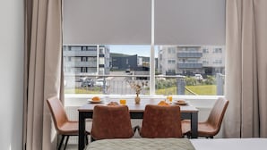 Uma área de refeições com mesa e cadeiras, um vaso com flores e vista para edifícios e rua.