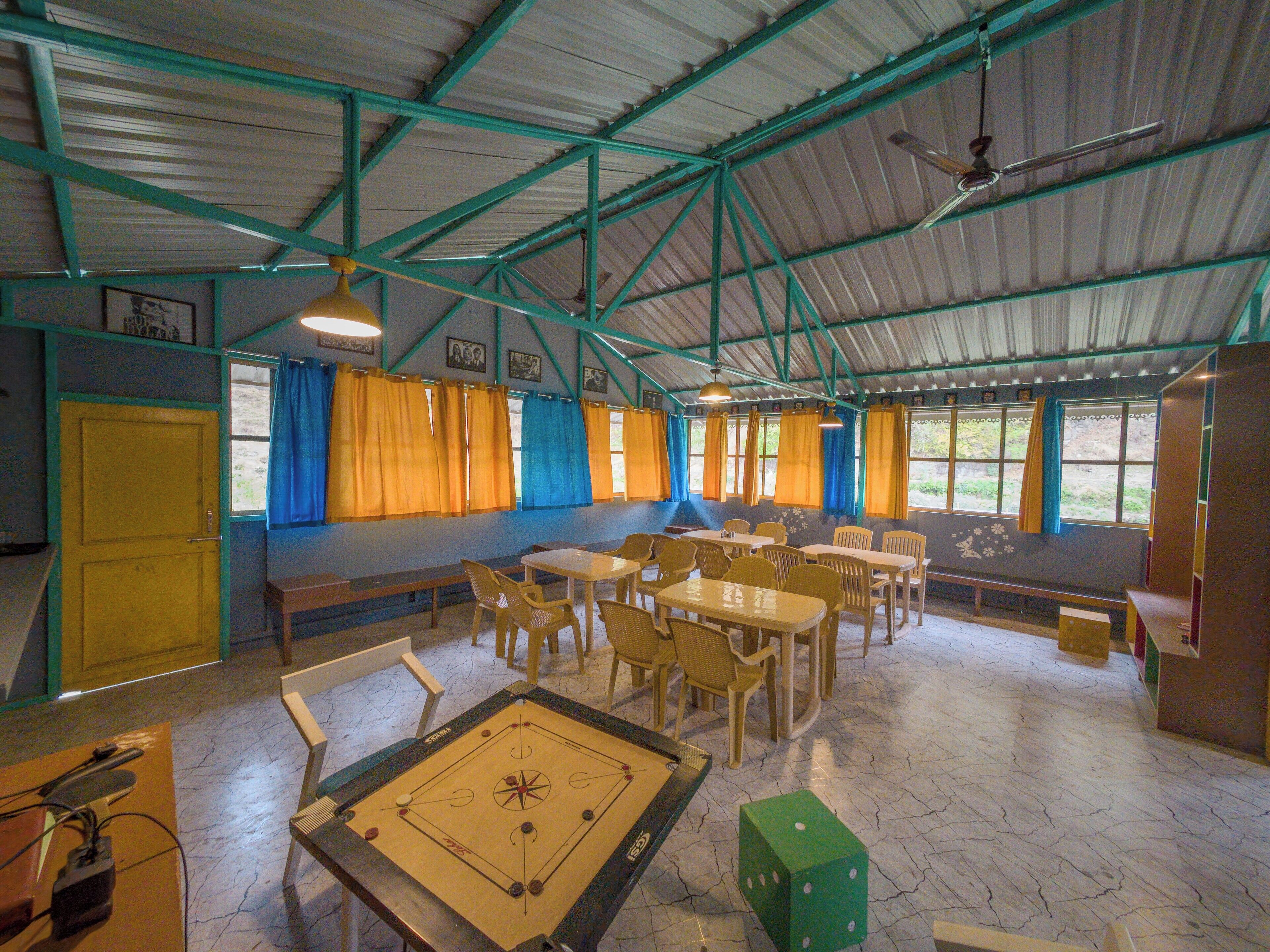Uma área de refeições com mesas e cadeiras, uma mesa de pebolim e um cubo verde.