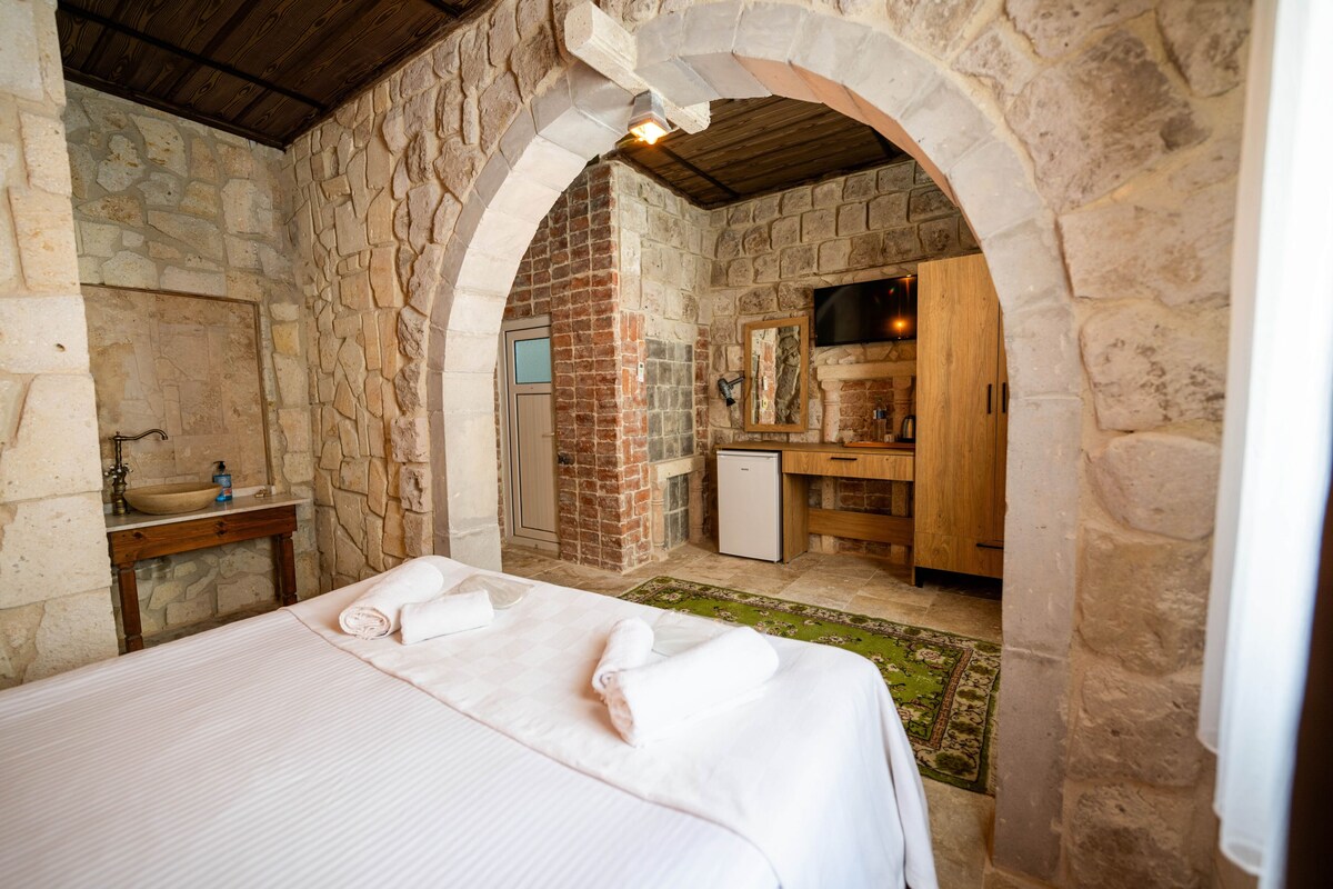 Quarto com paredes de pedra, uma cama, pia e uma pequena cozinha.