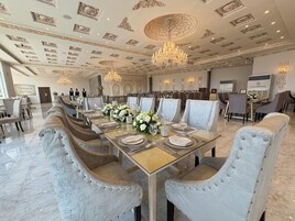 Uma sala de jantar formal com uma mesa longa posta para um banquete, cadeiras elegantes e um lustre.