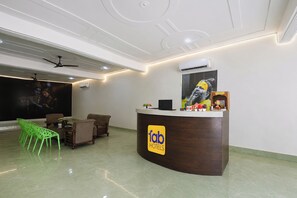Uma área de recepção de hotel com um balcão curvo, um ventilador de teto e um ar condicionado fixado na parede.
