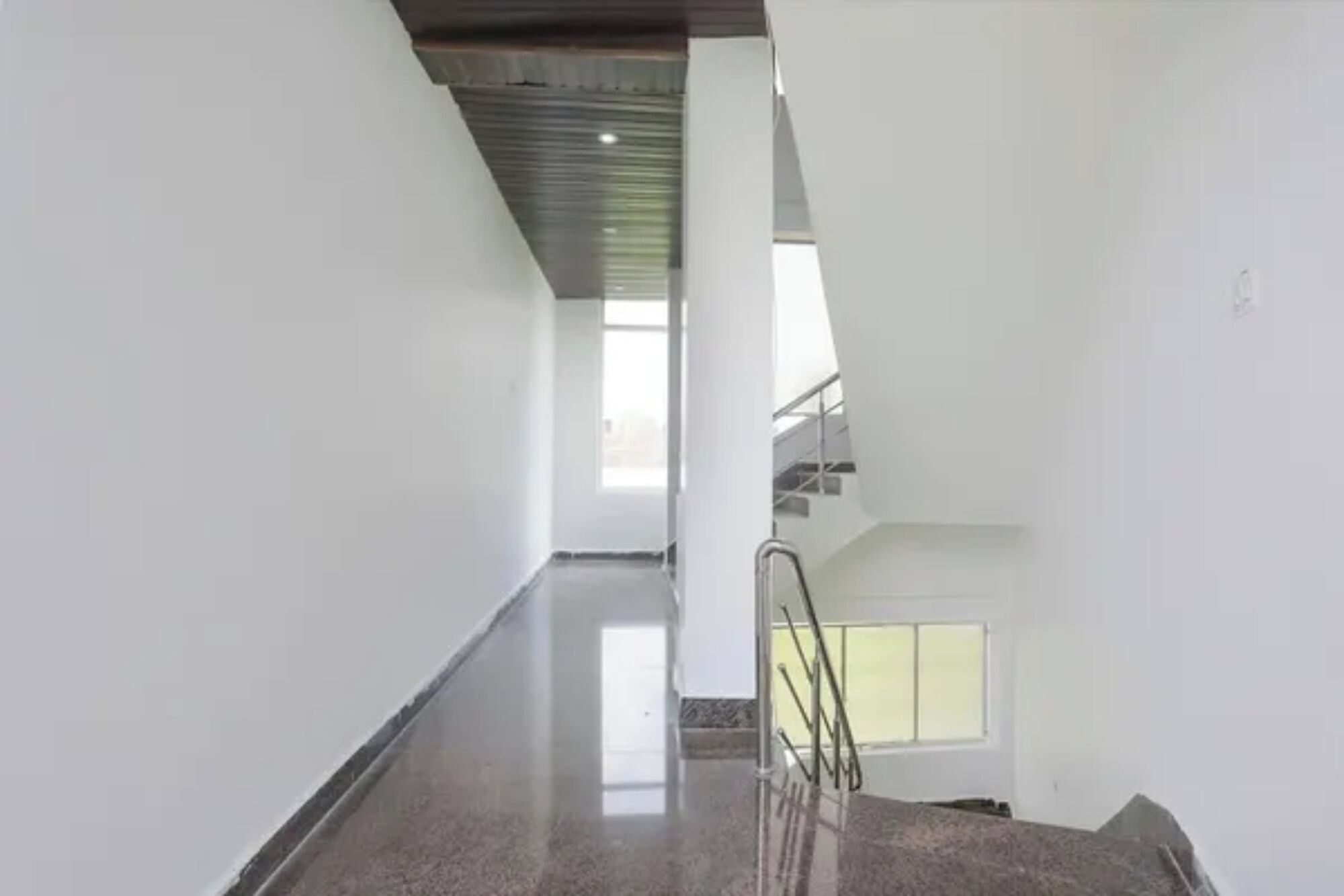 Um corredor com piso lustroso, paredes brancas e guarda-corpo de metal.