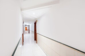 Um corredor longo e estreito, com paredes brancas e chão brilhante, que leva a uma porta no final.