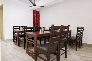 Uma área de refeições com uma mesa redonda e seis cadeiras, um ventilador de teto e uma cortina vermelha.