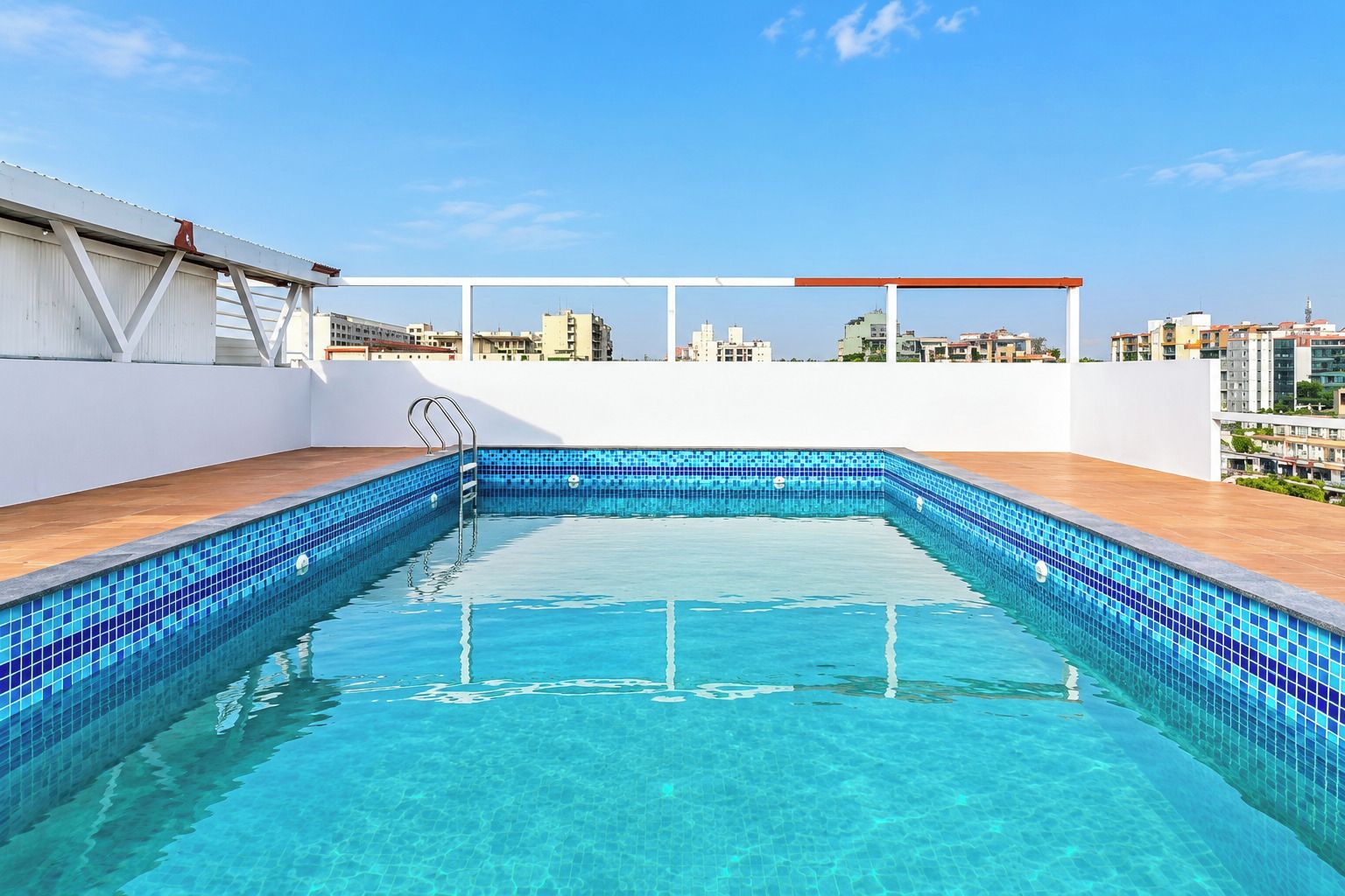 Piscina no terraço com água azul cristalina, rodeada por um muro branco e um deck de madeira.