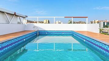 Piscina no terraço com água azul cristalina, rodeada por um muro branco e um deck de madeira.