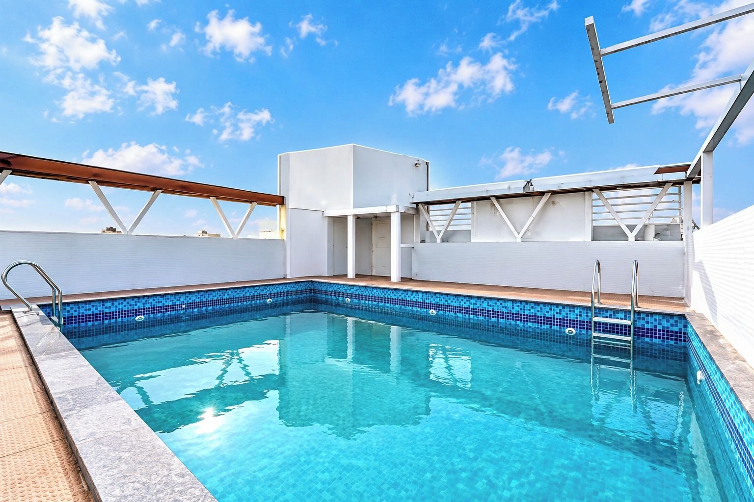 Piscina no terraço com água azul cristalina, rodeada por paredes brancas e um deck de madeira.