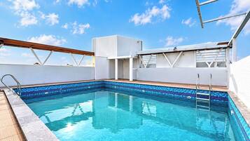 Piscina no terraço com água azul cristalina, rodeada por paredes brancas e um deck de madeira.