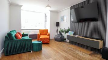 Uma sala de estar moderna com sofá, um banquinho e uma poltrona, uma TV de tela plana e um vaso de plantas.
