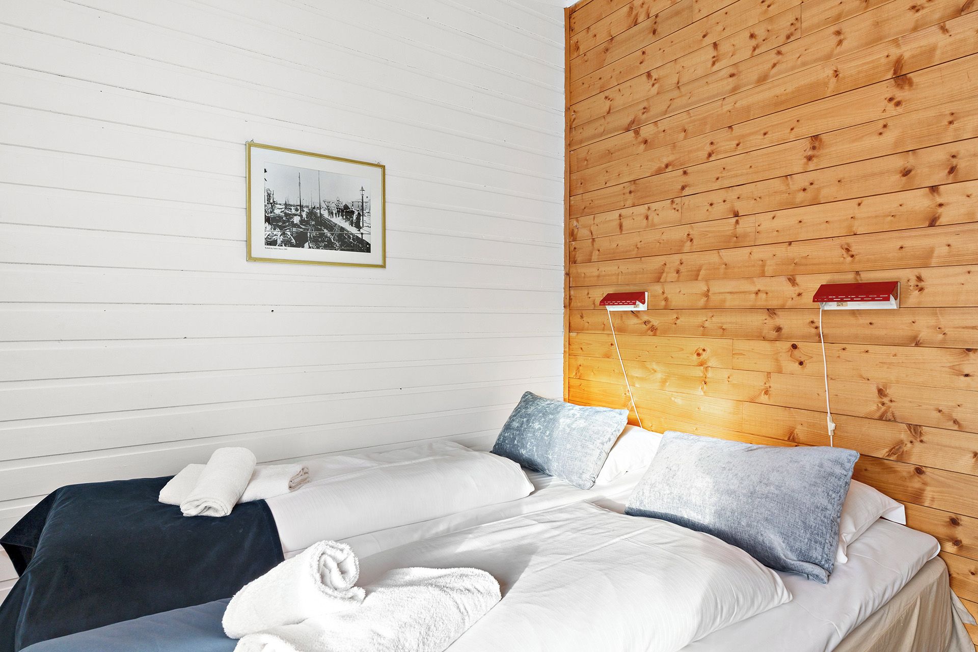 Quarto de hotel com cama, travesseiros, toalha, quadro na parede e painel de madeira.