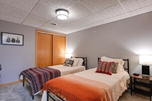 Quarto com duas camas, um guarda-roupa de madeira, mesa de cabeceira com abajur e um quadro na parede.