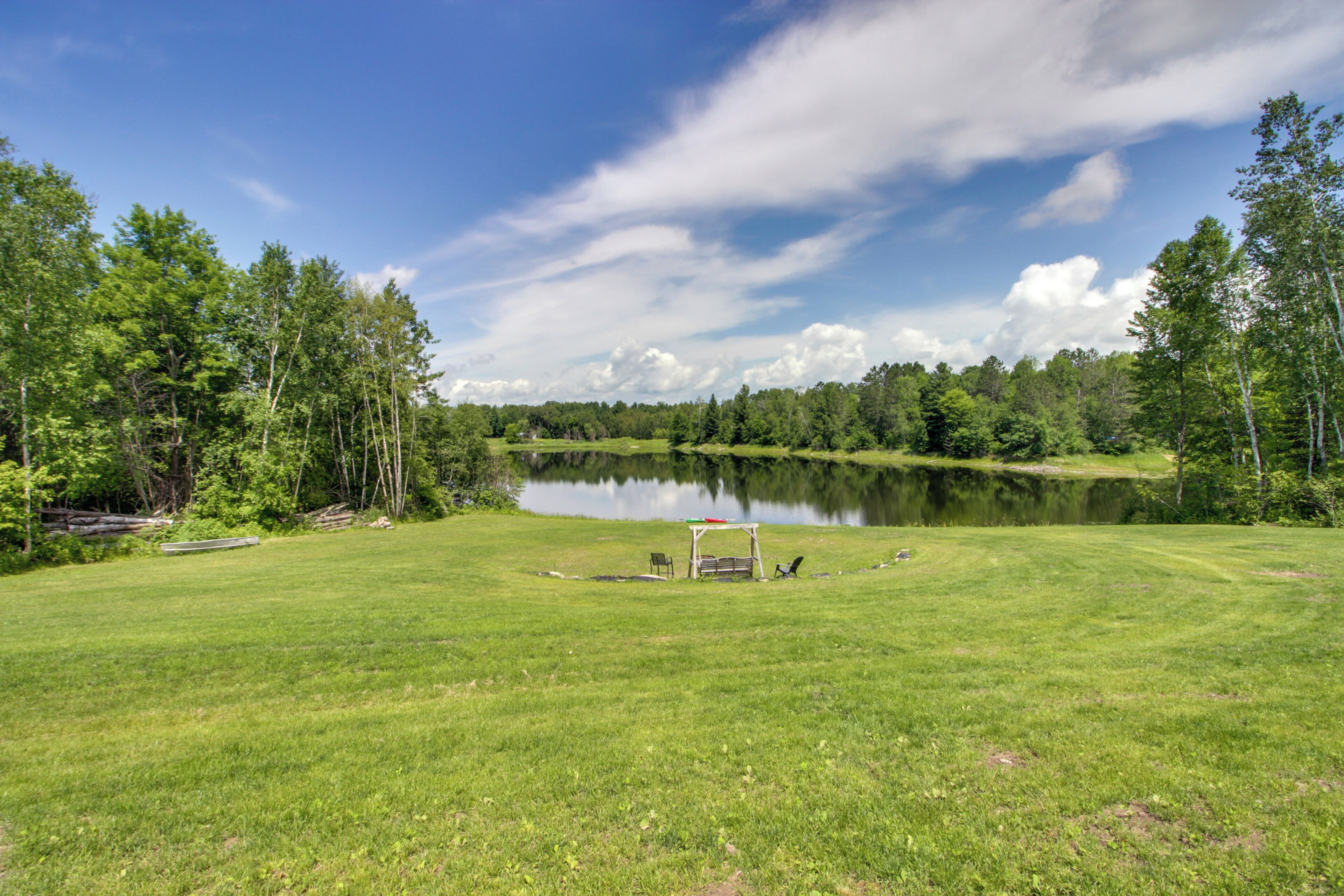 Um campo gramado com um banco e uma mesa, cercado por árvores e um lago.