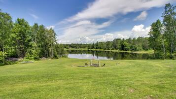 Um campo gramado com um banco e uma mesa, cercado por árvores e um lago.