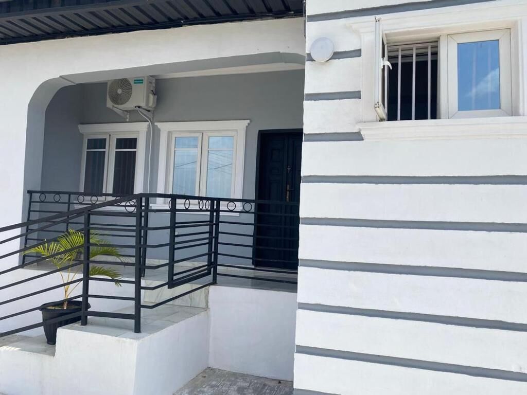 Edifício branco com escada de metal preta, um vaso de planta e uma janela com grade de segurança.