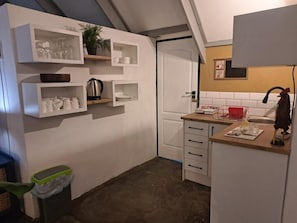 Uma cozinha compacta com armários brancos, uma pia e um balcão com uma chaleira e uma planta.