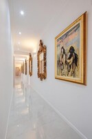 Um corredor com piso lustroso, uma série de obras de arte emolduradas nas paredes, e uma grande pintura representando cavalos.