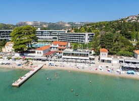 Um hotel à beira-mar com vários andares, um píer que se estende para o mar e uma área de praia com guarda-sóis e espreguiçadeiras.