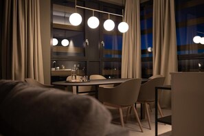 Uma área de jantar moderna com mesa, cadeiras e luminárias pendentes.