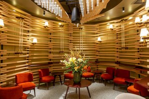 Um interior moderno com ripas de madeira nas paredes, cadeiras estofadas em vermelho e uma mesa central com um arranjo floral.
