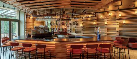 Uma área de bar moderna com uma ilha central, banquetas e uma variedade de garrafas e copos.