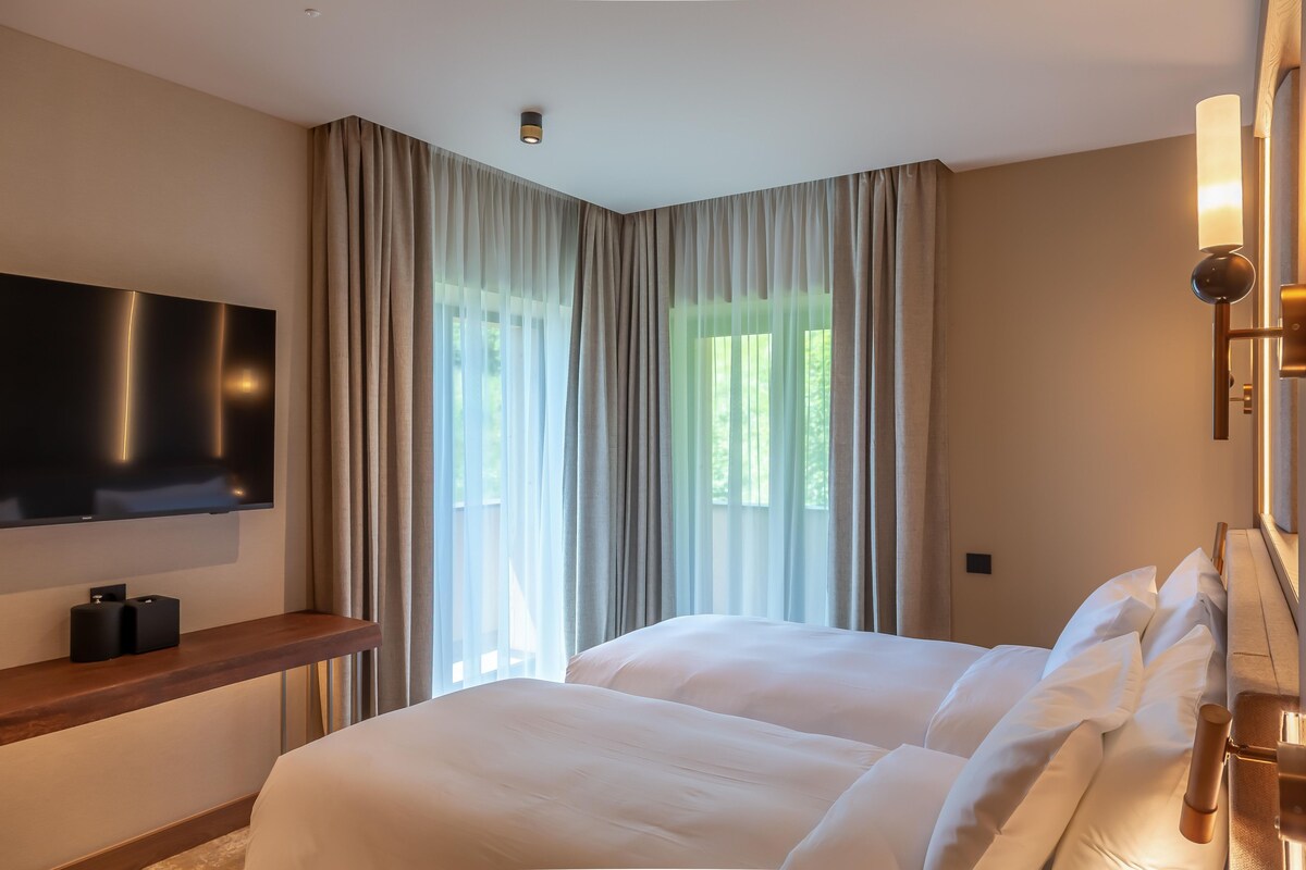Quarto de hotel com uma cama grande, televisão de tela plana na parede e uma janela com cortinas.