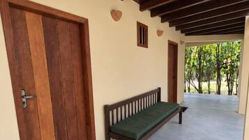 Área externa coberta com banco de madeira, uma porta e vista para o verde.