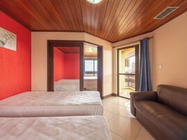 Quarto com duas camas, um sofá de couro marrom, uma parede vermelha e uma varanda com vista.