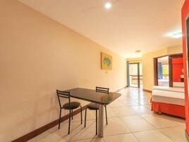 Quarto de hotel com cama, mesa de jantar com cadeiras, um quadro na parede e uma porta que dá para outro cômodo.