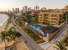 Um hotel à beira-mar com piscina, assentos na praia e um horizonte urbano ao fundo.