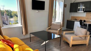 Uma sala de estar moderna com sofá, poltronas, mesa de centro e uma área de cozinha com micro-ondas e armários.