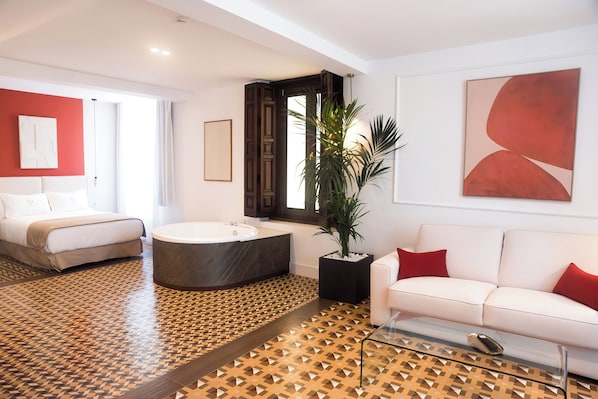 Quarto de hotel moderno com uma cama, área de estar com sofá, mesa de centro de vidro, uma planta grande em vaso e uma banheira.