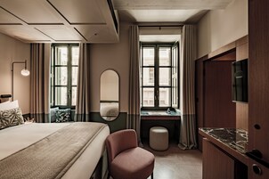 Quarto de hotel com cama, escrivaninha, cadeira, espelho e televisão.