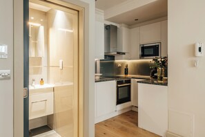 Cozinha moderna com armários brancos, forno embutido, micro-ondas e box de vidro.