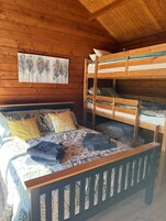 Quarto de cabana de madeira com beliches, uma cama com roupa de cama floral e um quadro na parede.
