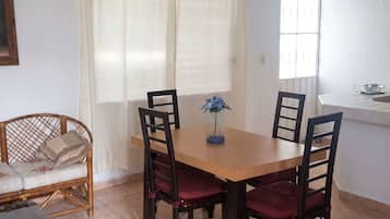 Uma sala de jantar com mesa de madeira e quatro cadeiras, um sofá de vime e uma janela com cortinas.