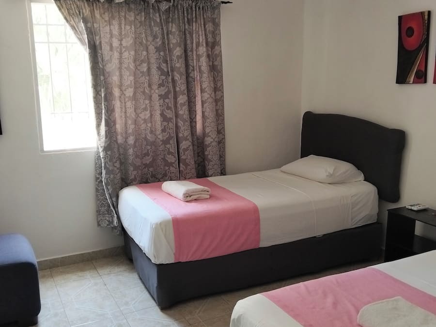 Quarto com cama, mesa de cabeceira, janela com cortinas e ar-condicionado fixado na parede.