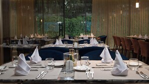 Um restaurante com várias mesas preparadas para refeições, com vista para o verde através de grandes janelas.