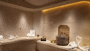 Um quarto de spa com parede em mosaico, uma bacia de pedra e toalhas.