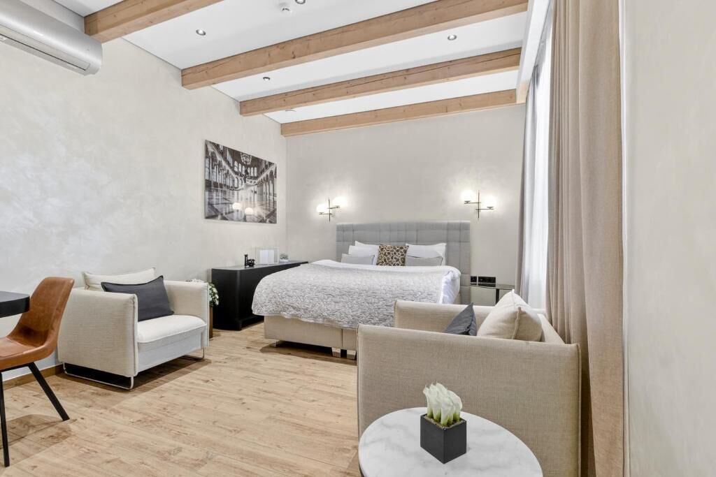 Quarto de hotel moderno com cama, sofá, poltrona, mesinha e um quadro na parede.