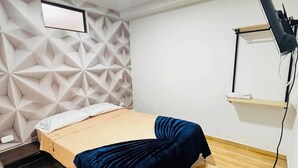 Quarto com uma cama, televisão fixada na parede e chão de madeira.