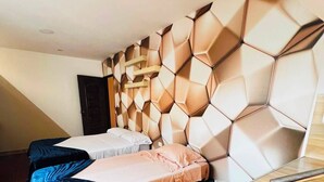 Quarto de hotel com design moderno, apresentando uma cabeceira com padrão hexagonal, uma mesa de jantar de madeira com pia e piso de azulejos vermelhos.