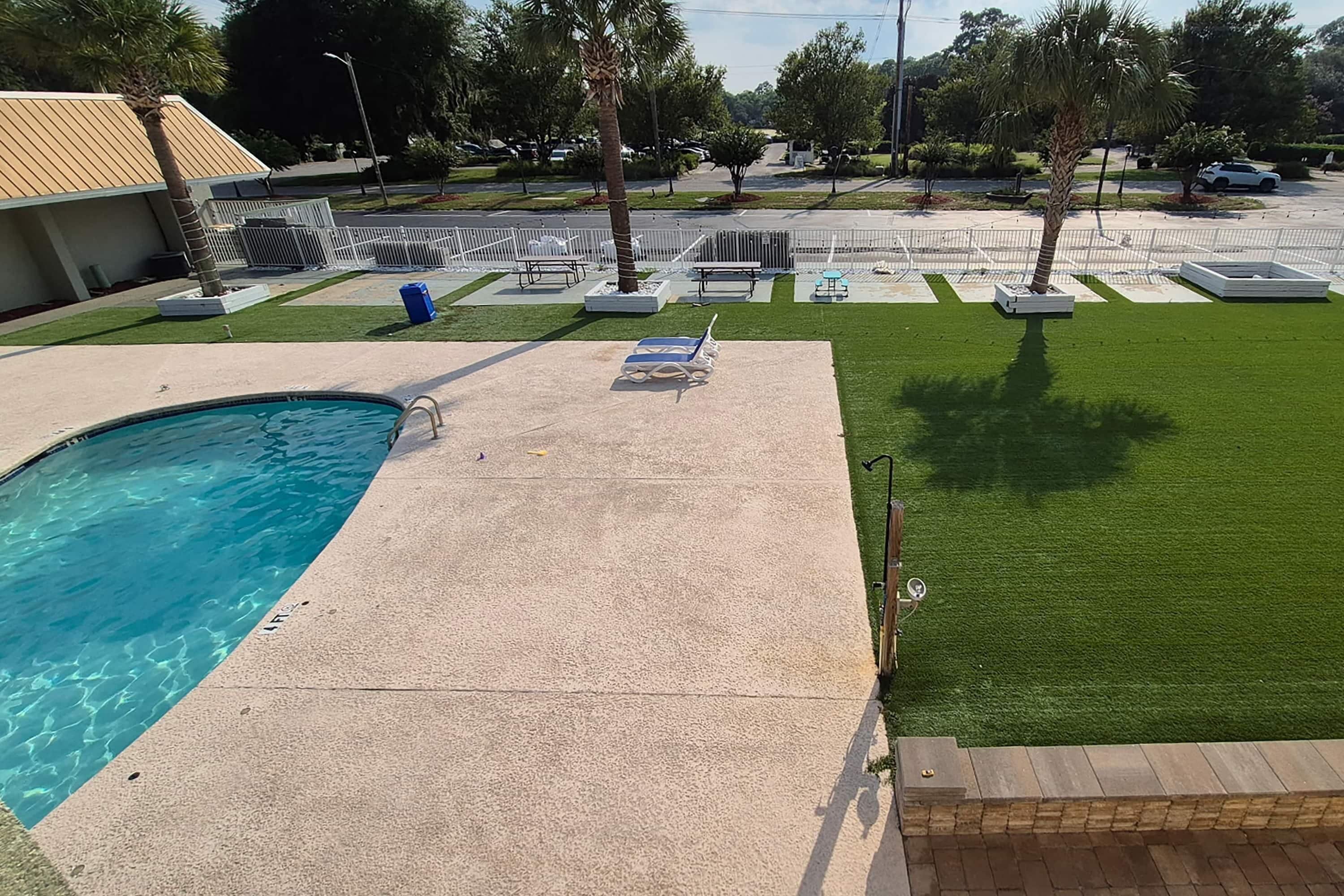 Piscina com deck de concreto, cercada por um gramado bem cuidado e algumas árvores.