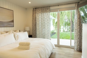 Quarto com uma cama grande, uma mesa de cabeceira, um abajur e vista para um jardim através de uma porta de correr.