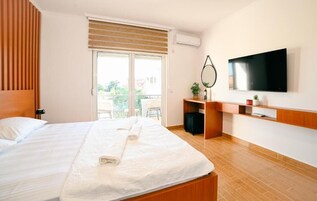 Quarto de hotel com uma cama, televisão, escrivaninha e janela com persianas.