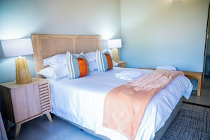 Cama bem arrumada com almofadas, abajur e mesa de cabeceira de madeira.