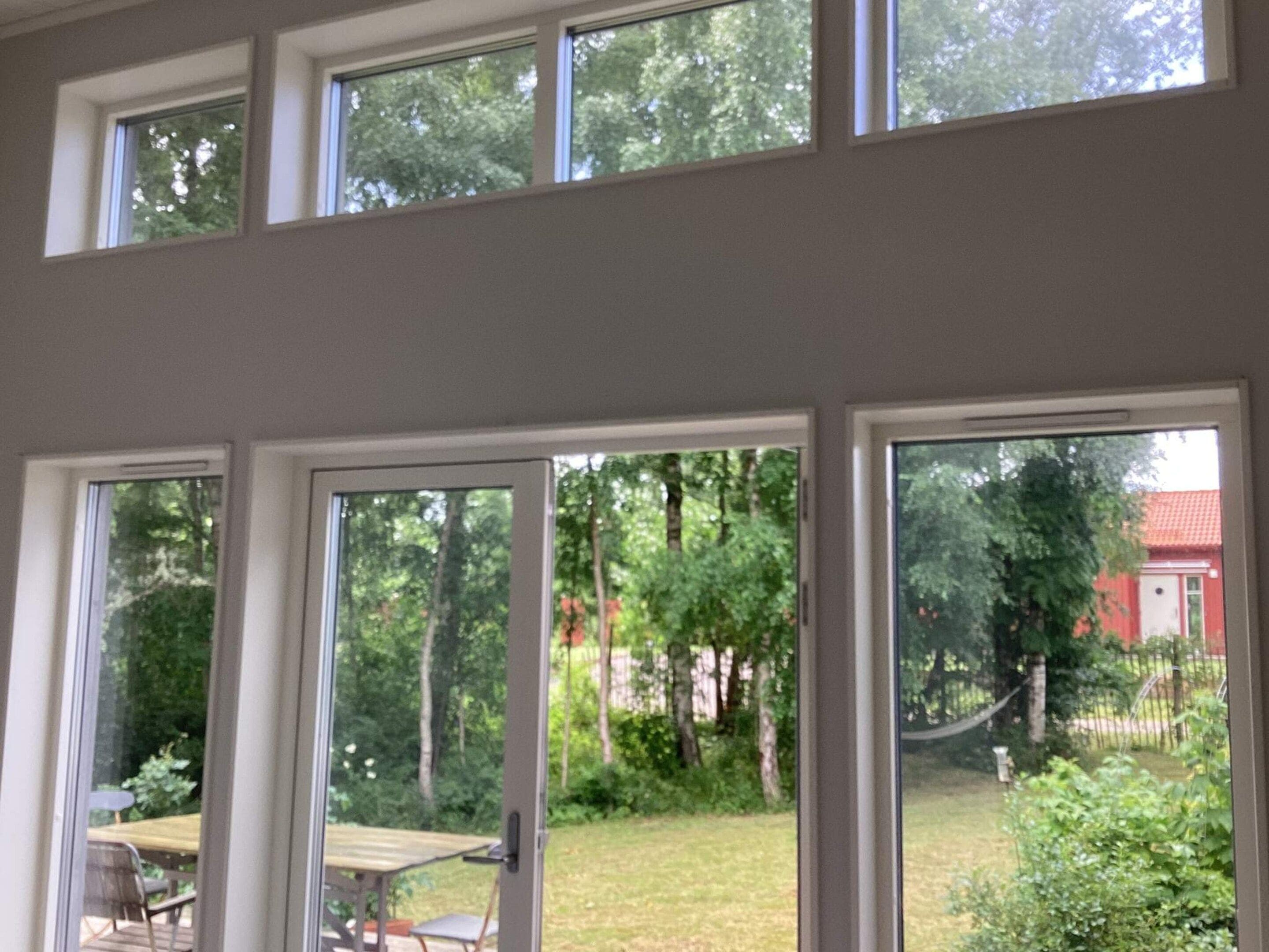 Quarto com grandes janelas que oferecem vista para um jardim e um edifício vermelho.