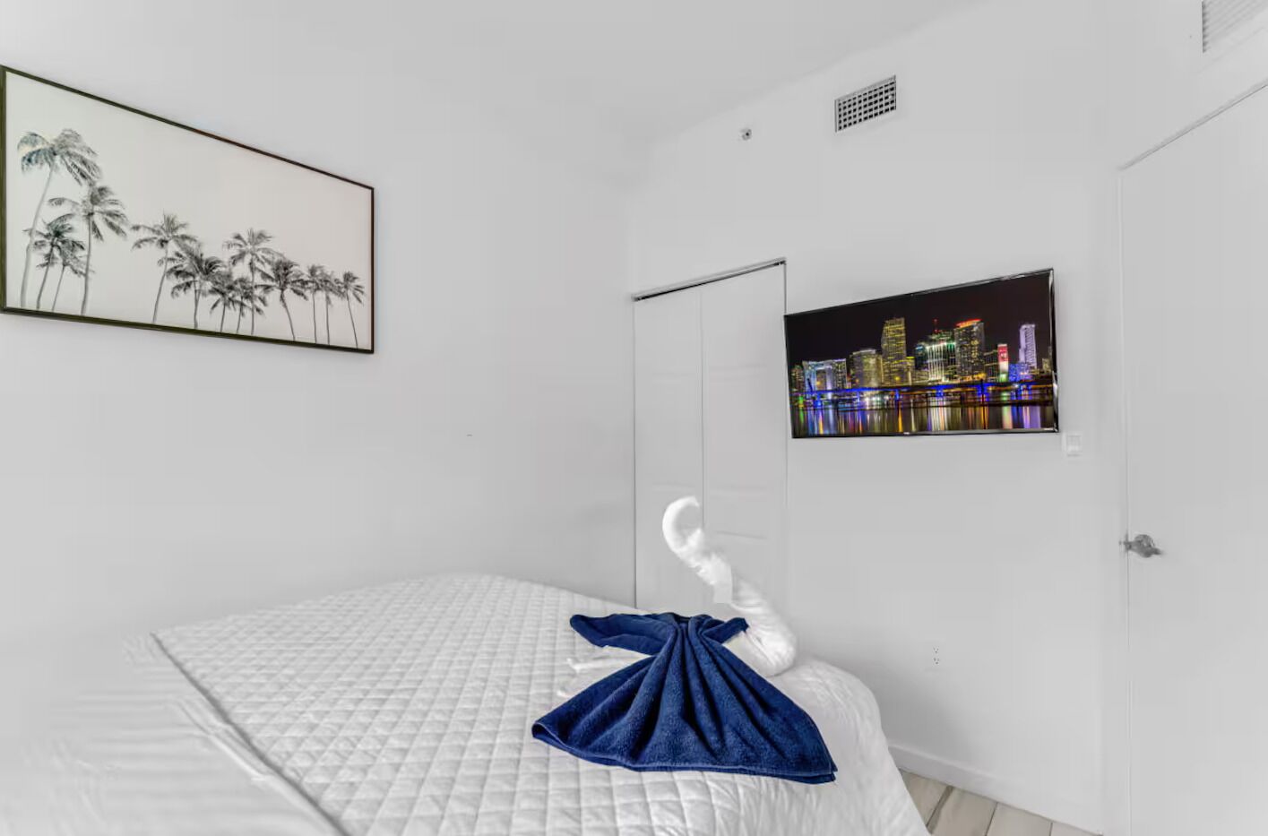 Quarto com cama, quadro de paisagem urbana e porta branca.
