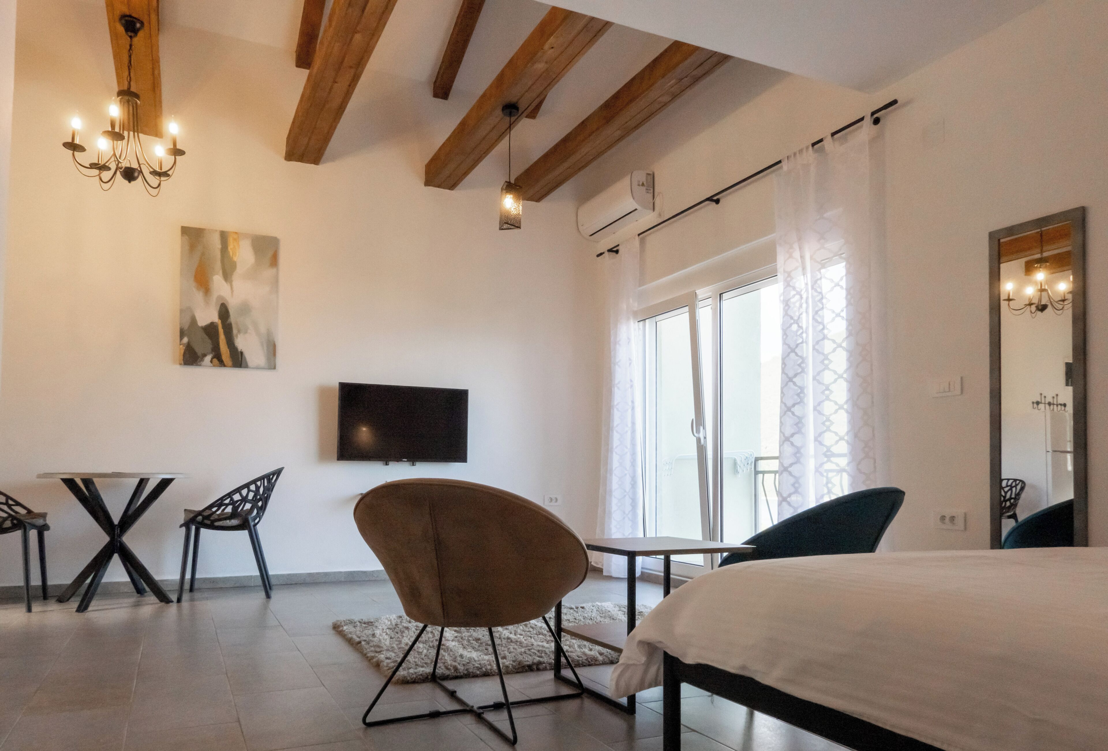 Quarto moderno com cama, televisão, área de refeições com cadeiras e um candelabro.