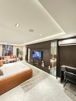 Quarto de hotel moderno com uma cama grande, televisão na parede, um sofá e um espaço de trabalho.