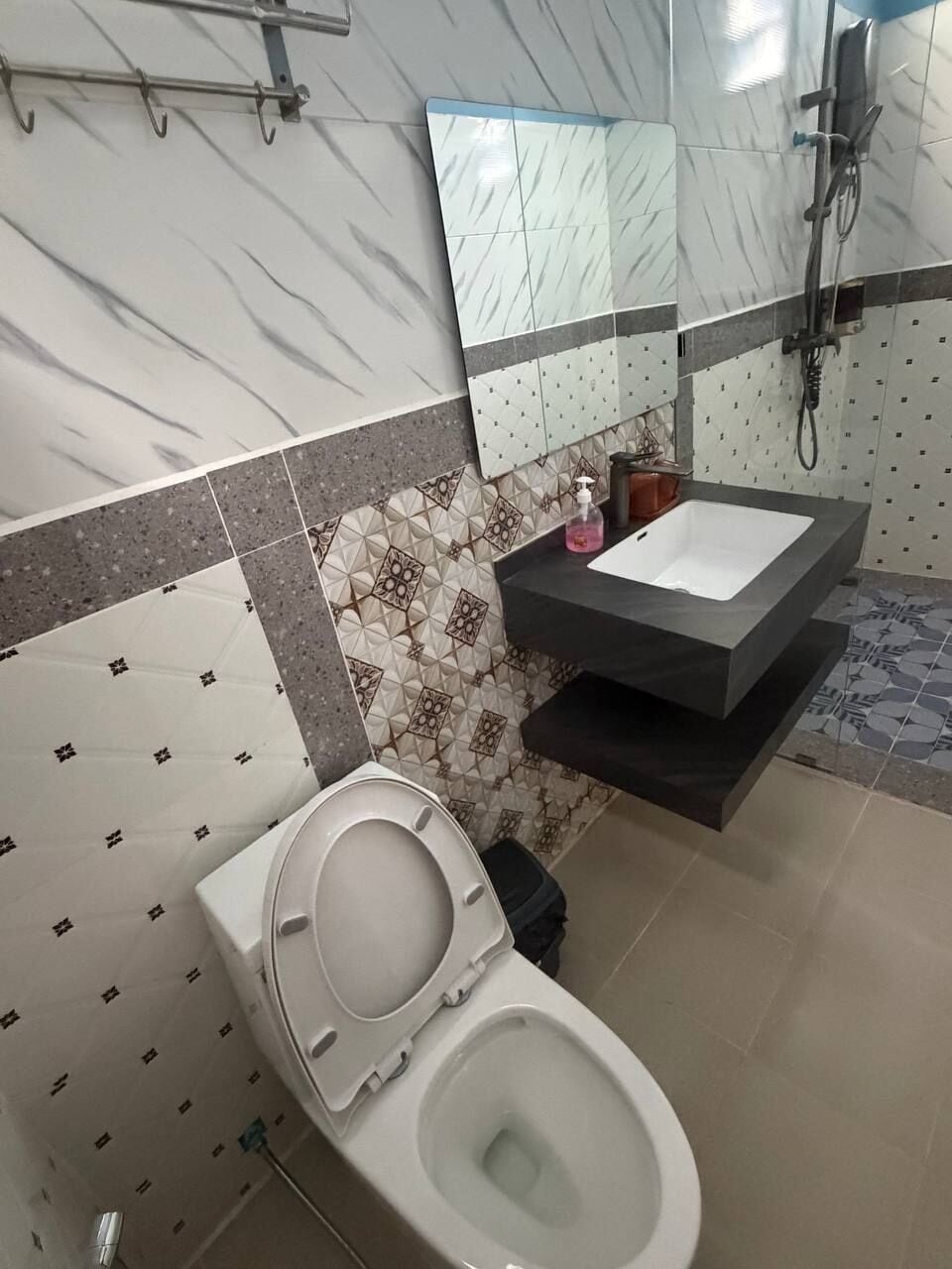 Uma casa de banho com sanita branca, lavatório preto, espelho e chuveiro.